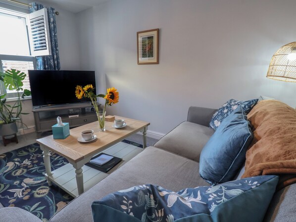 Uma sala de estar com sofá, mesa de centro, televisão e um vaso de planta.