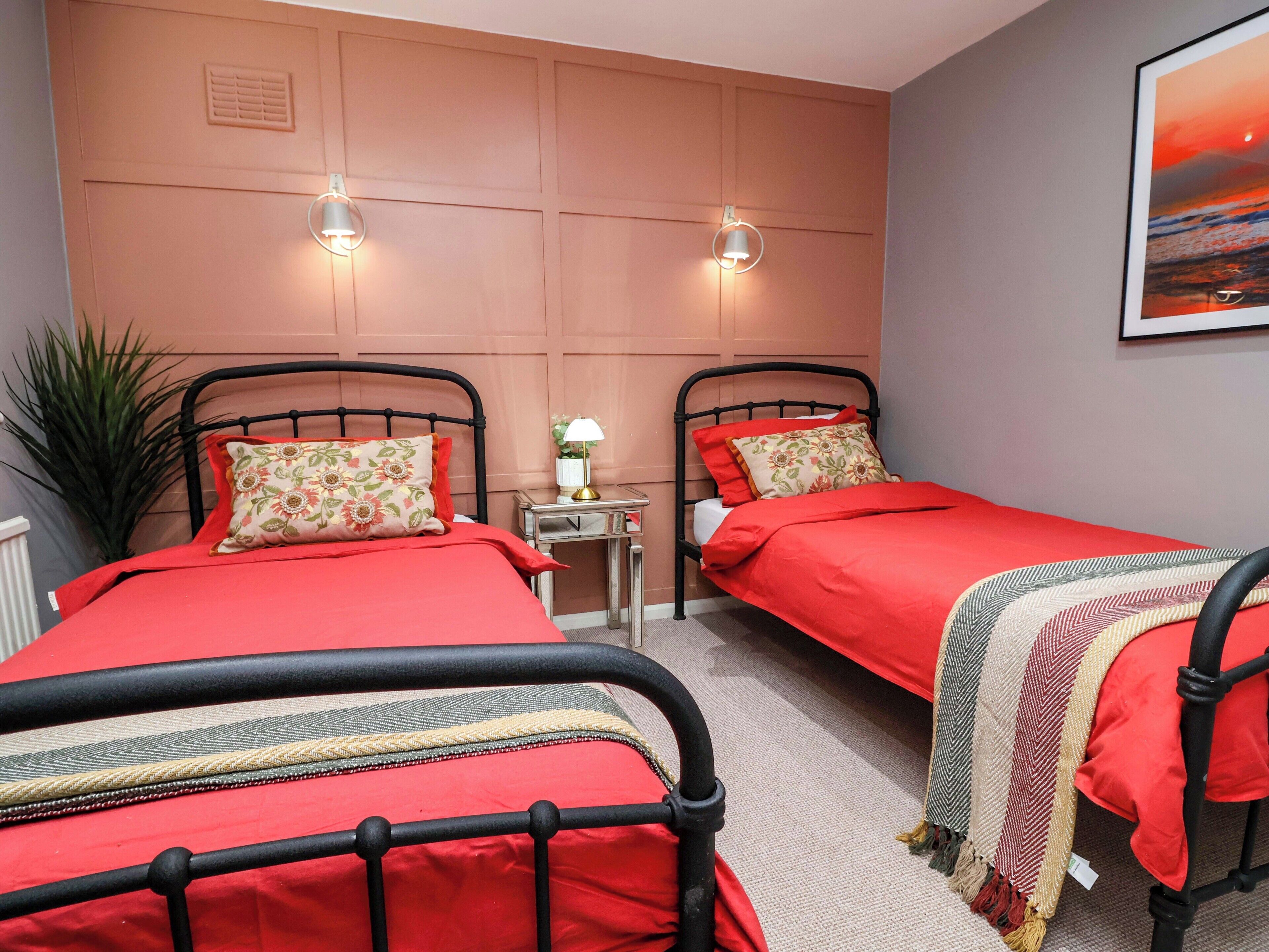Quarto com duas camas, uma mesa de cabeceira, uma luminária e um quadro na parede.