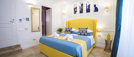 Quarto de hotel com uma cama grande, um espelho, uma TV fixada na parede e uma pequena mesa de apoio.