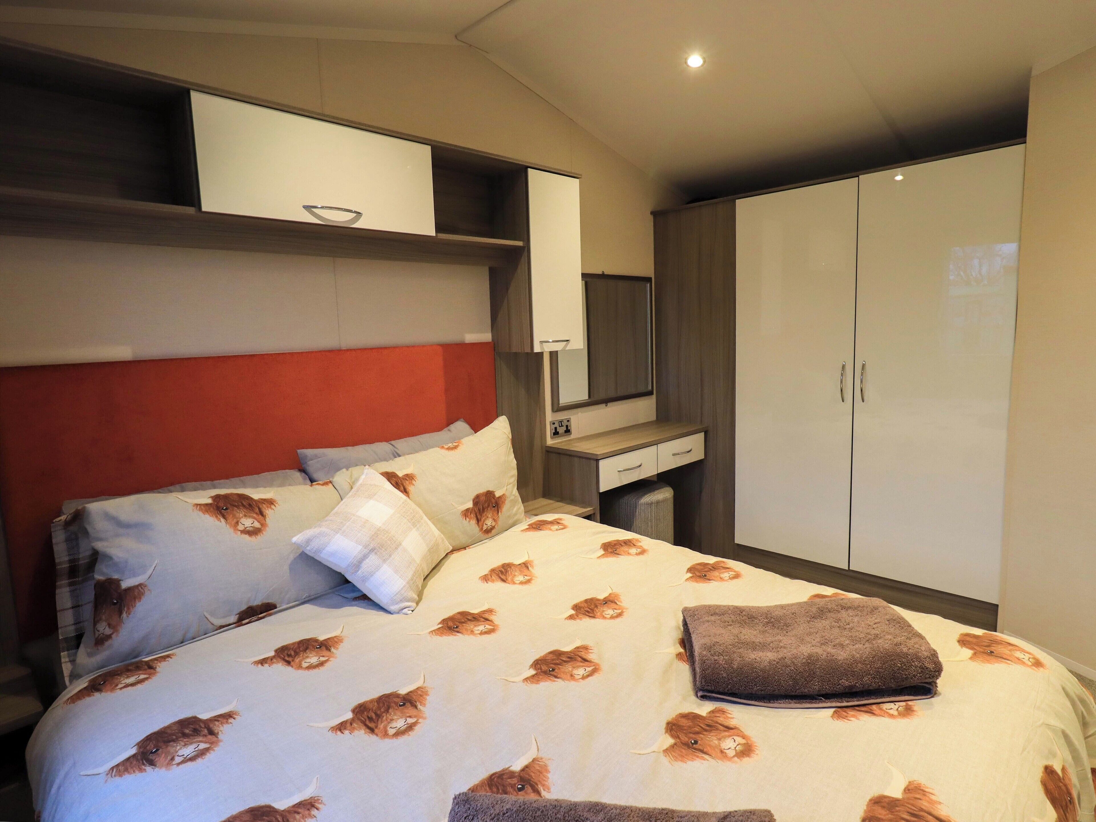 Quarto de hotel com cama, escrivaninha, guarda-roupa e espelho.