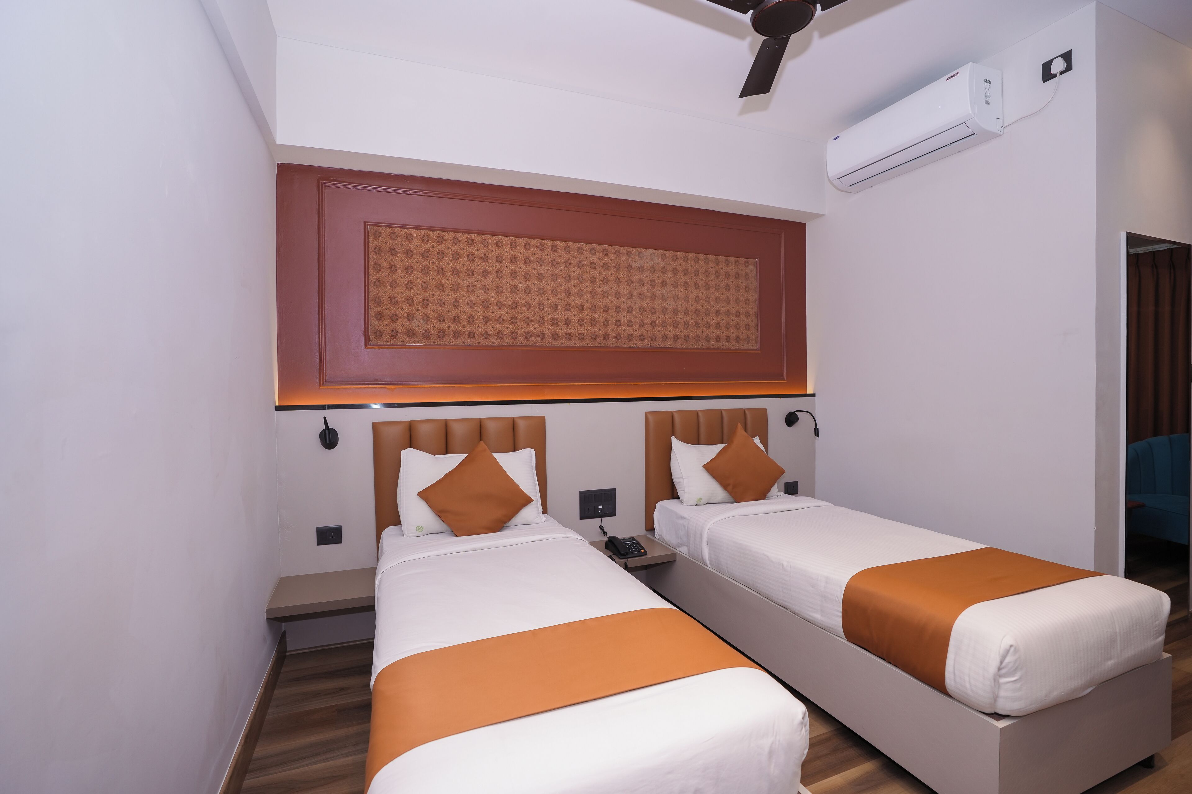 Quarto de hotel com duas camas de solteiro, piso de madeira, ventoinha no teto e ar condicionado.
