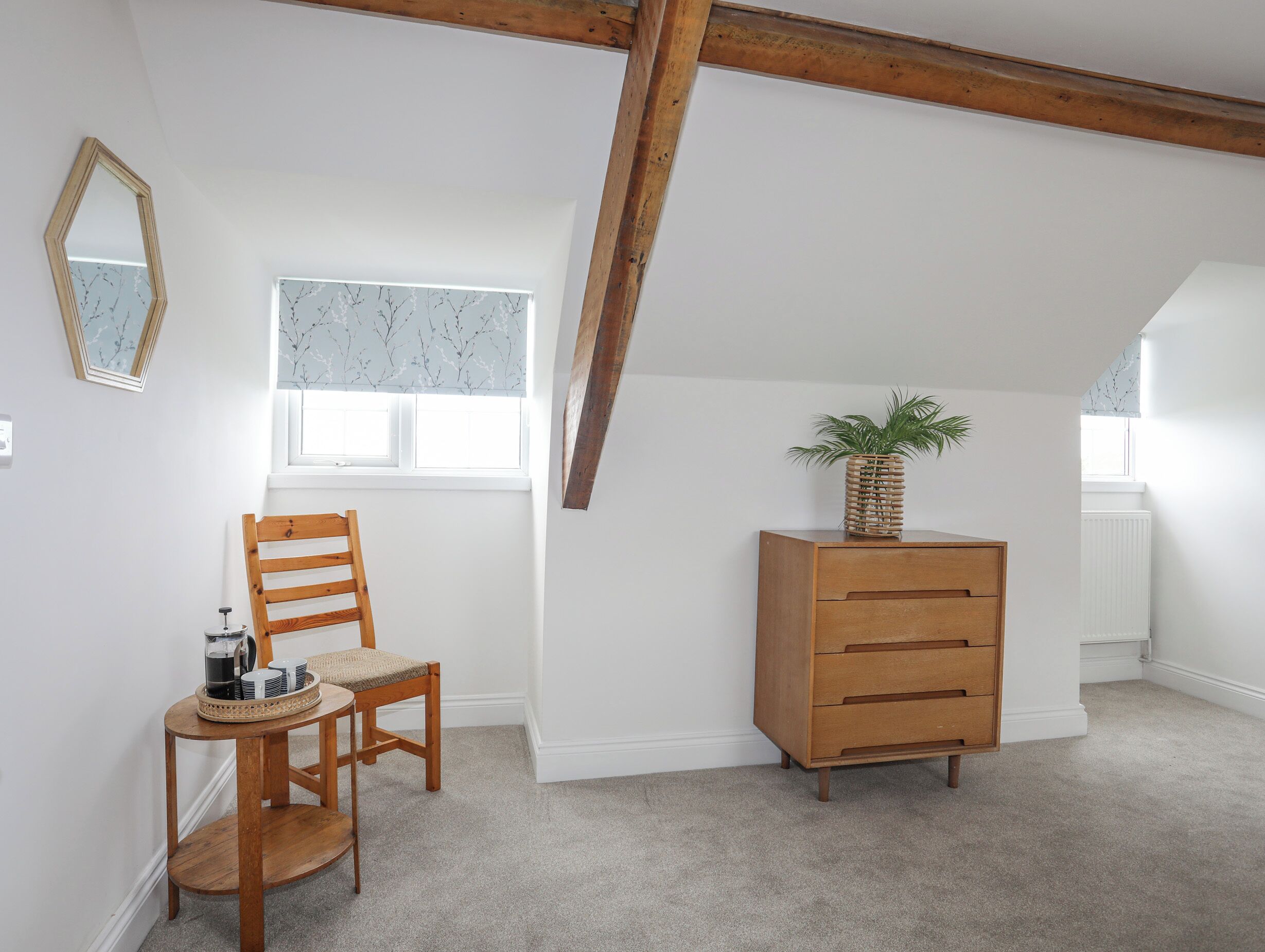 Um quarto com uma cadeira de madeira, uma mesa pequena com um tabuleiro, um aparador e um espelho na parede.
