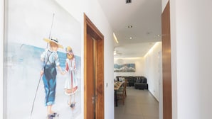 Um corredor com uma porta de madeira, uma sala de jantar com mesa e cadeiras, e uma sala de estar com sofá e um quadro na parede.