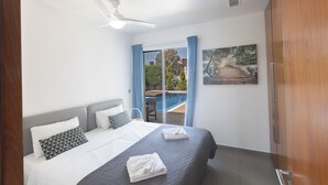Quarto moderno com cama, ventilador de teto, pintura e vista para uma piscina através de uma porta de vidro.