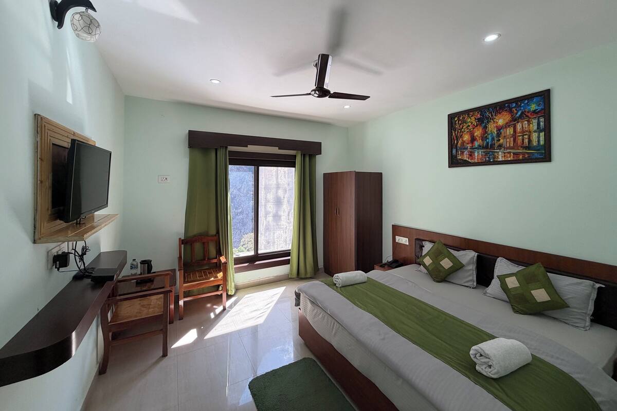Quarto de hotel com cama, escrivaninha, cadeira, guarda-roupa, quadro e ventilador de teto.