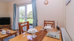 Uma sala de jantar com mesa de madeira, cadeiras, televisão e relógio na parede.