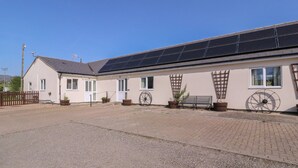 Um edifício com telhado solar, entrada por um caminho de cascalho e área cercada.