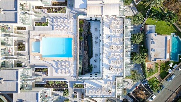 Vista aérea de um hotel moderno com piscina central, várias varandas e áreas de estar ao ar livre.