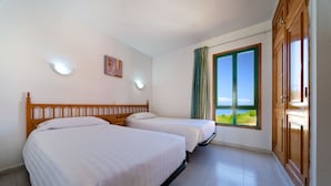 Quarto de hotel com duas camas, uma janela com cortinas, um guarda-roupa de madeira e um aplique na parede.