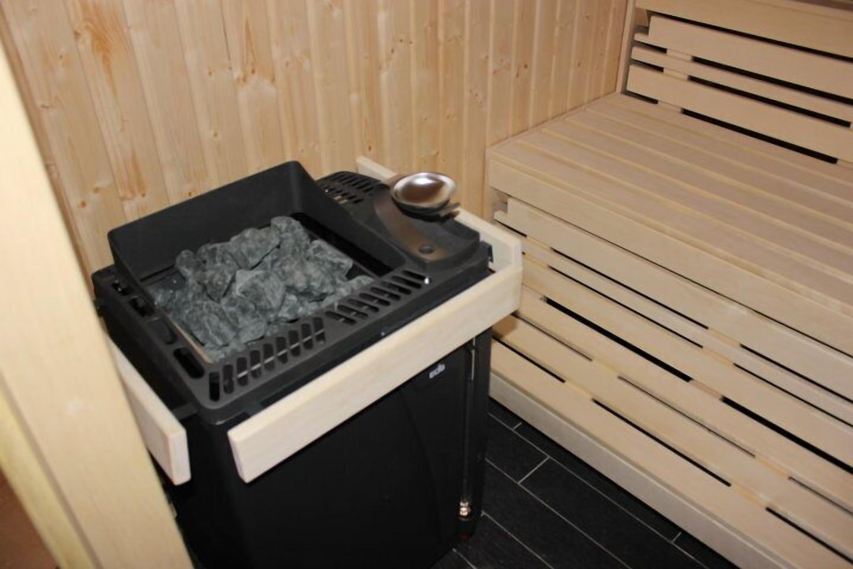 Uma sauna com aquecedor preto, painel de controle e banco de madeira.