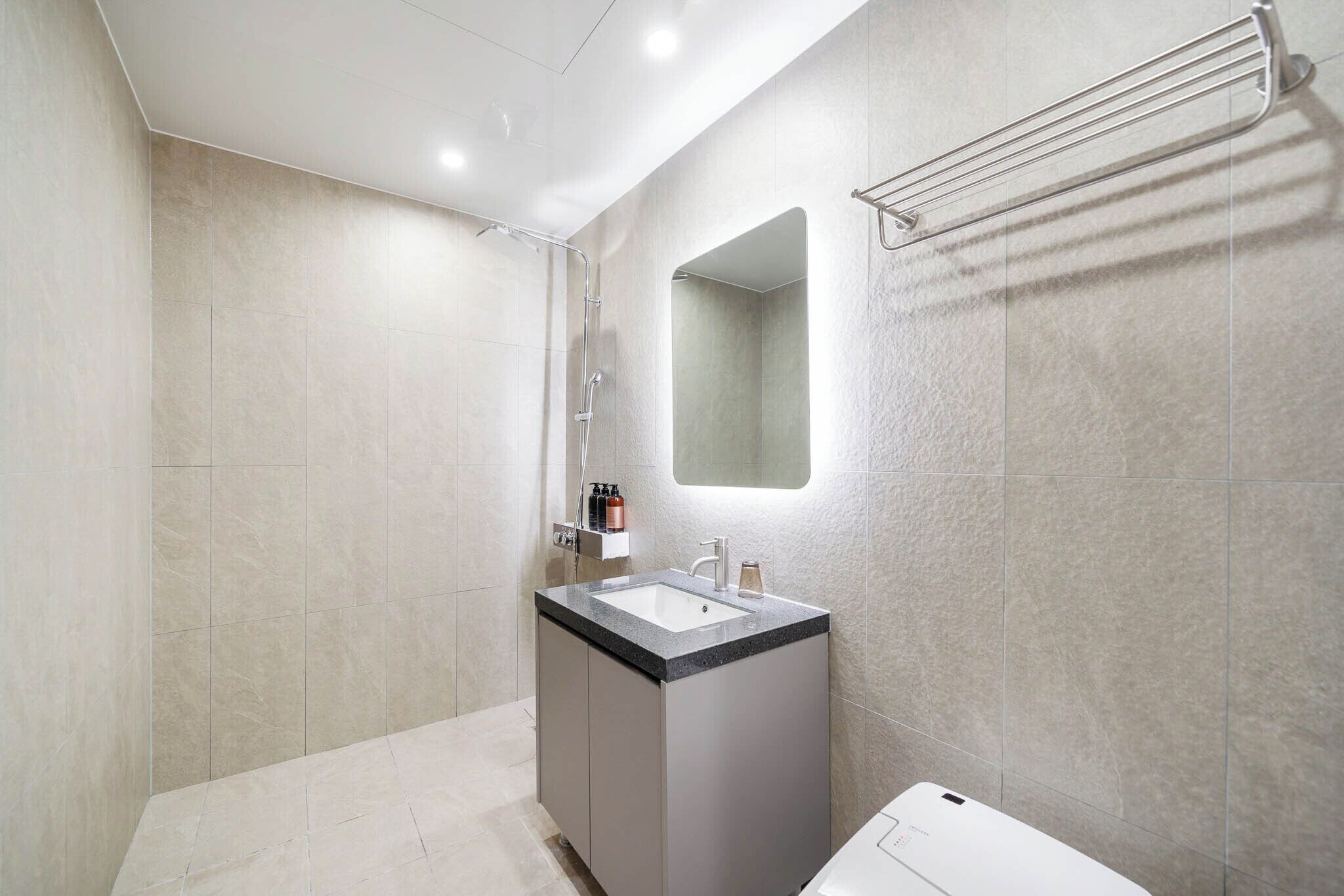 Uma casa de banho moderna com chuveiro, lavatório com espelho e um porta-toalhas.