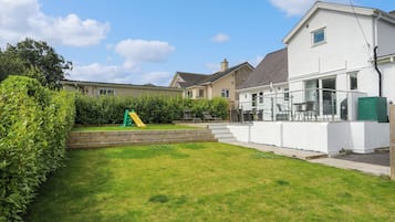Um quintal residencial com gramado, área de recreação infantil com escorregador, e uma casa branca com varanda.