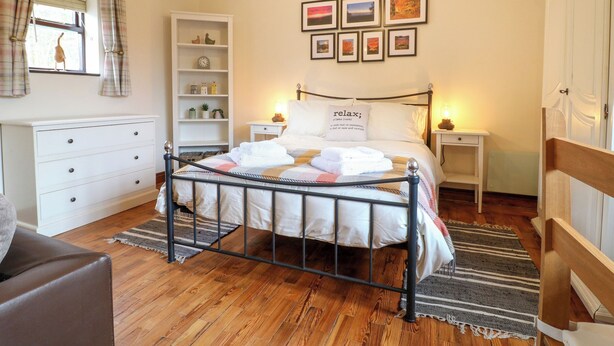 Quarto com cama, penteadeira, mesa de cabeceira, prateleira com objetos decorativos e parede com quadros.