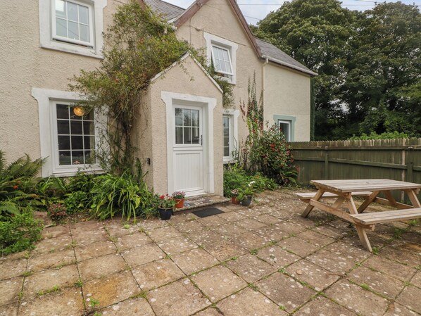 Uma casa com porta, janelas e um jardim com plantas e uma mesa de madeira.