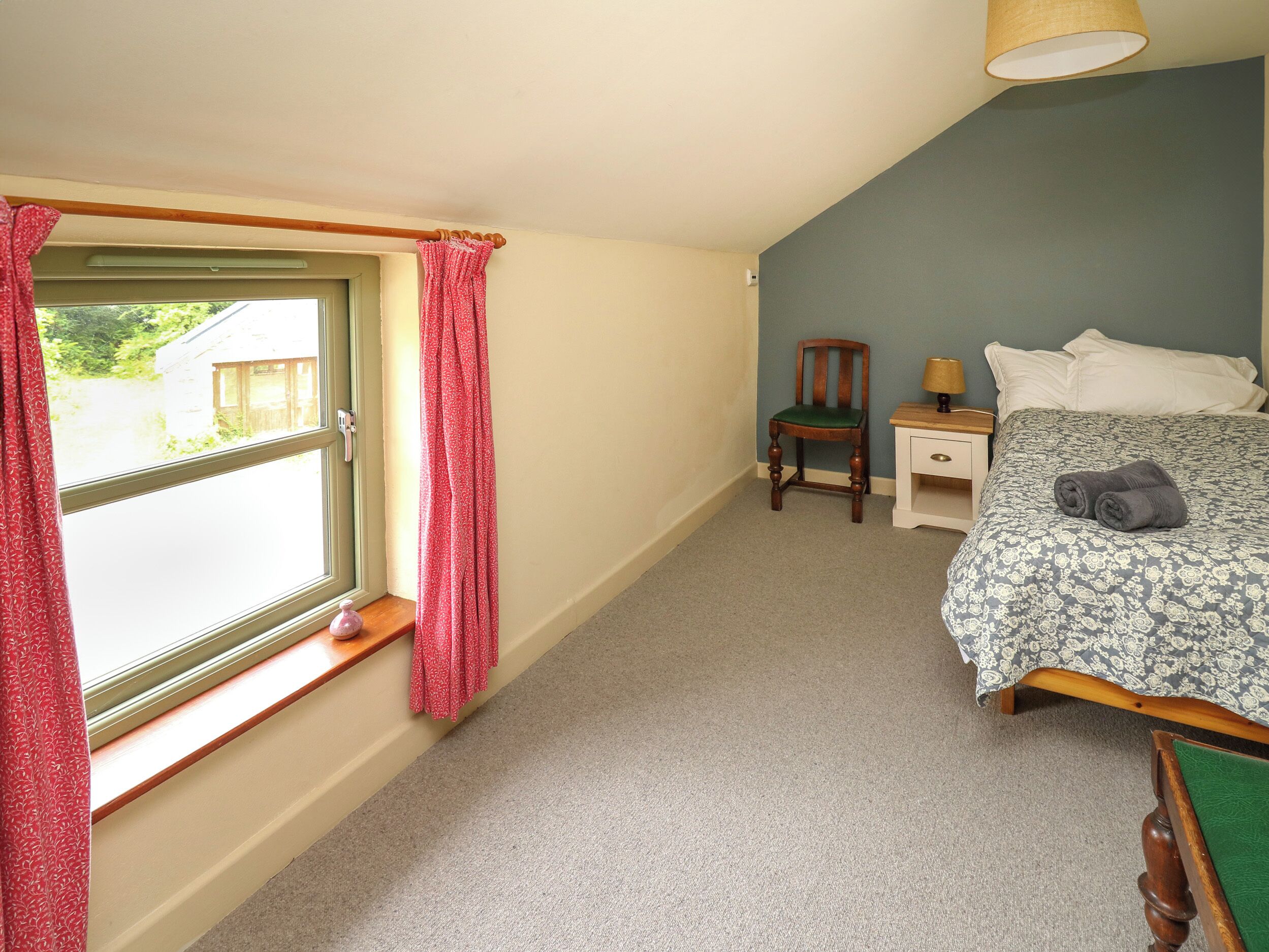 Quarto com cama, cadeira, mesa de cabeceira, luminária e janela com cortinas.