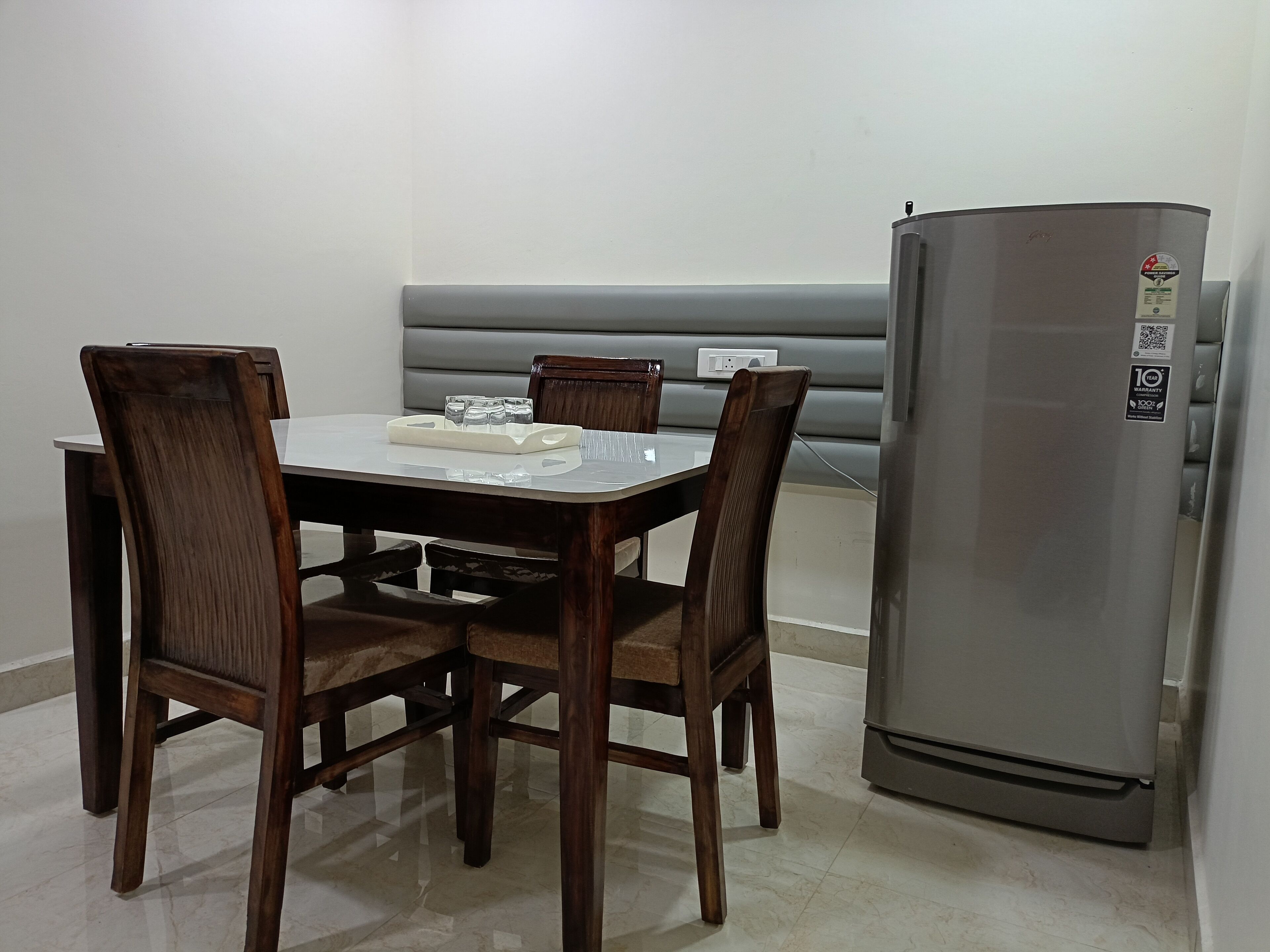 Uma sala de jantar com mesa, cadeiras, geladeira e um sofá cinza.