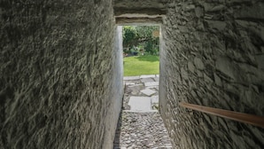 Um corredor de pedra com corrimão de madeira, que leva a um jardim ao ar livre.