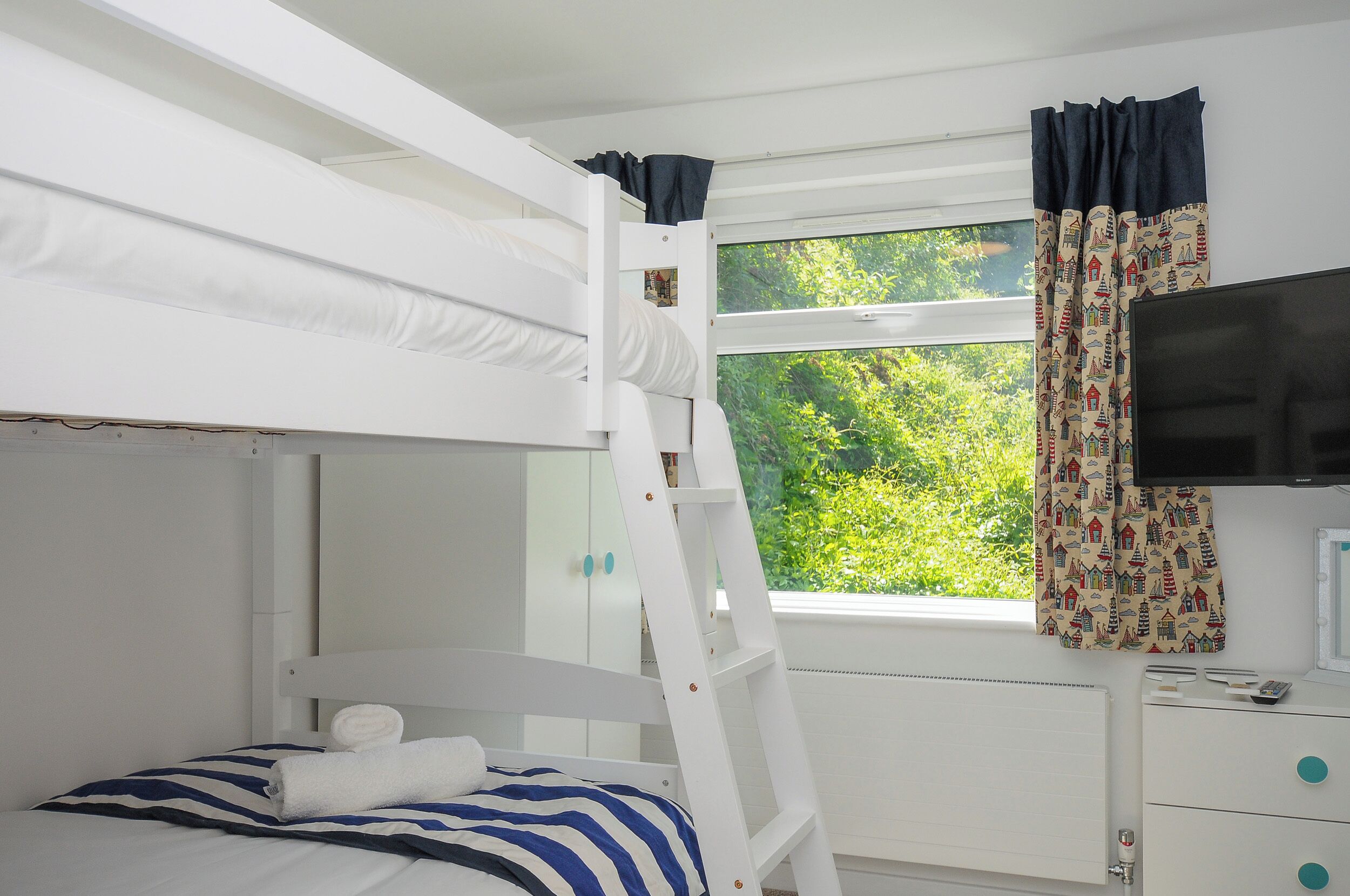 Uma cama beliche com escada, uma televisão e uma janela com cortinas.