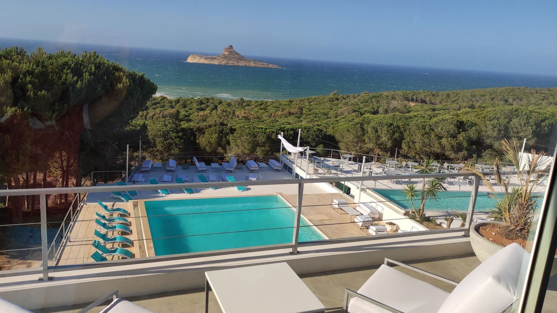 Área de piscina no terraço com várias piscinas e espreguiçadeiras, cercada por vegetação exuberante e vista para o mar.