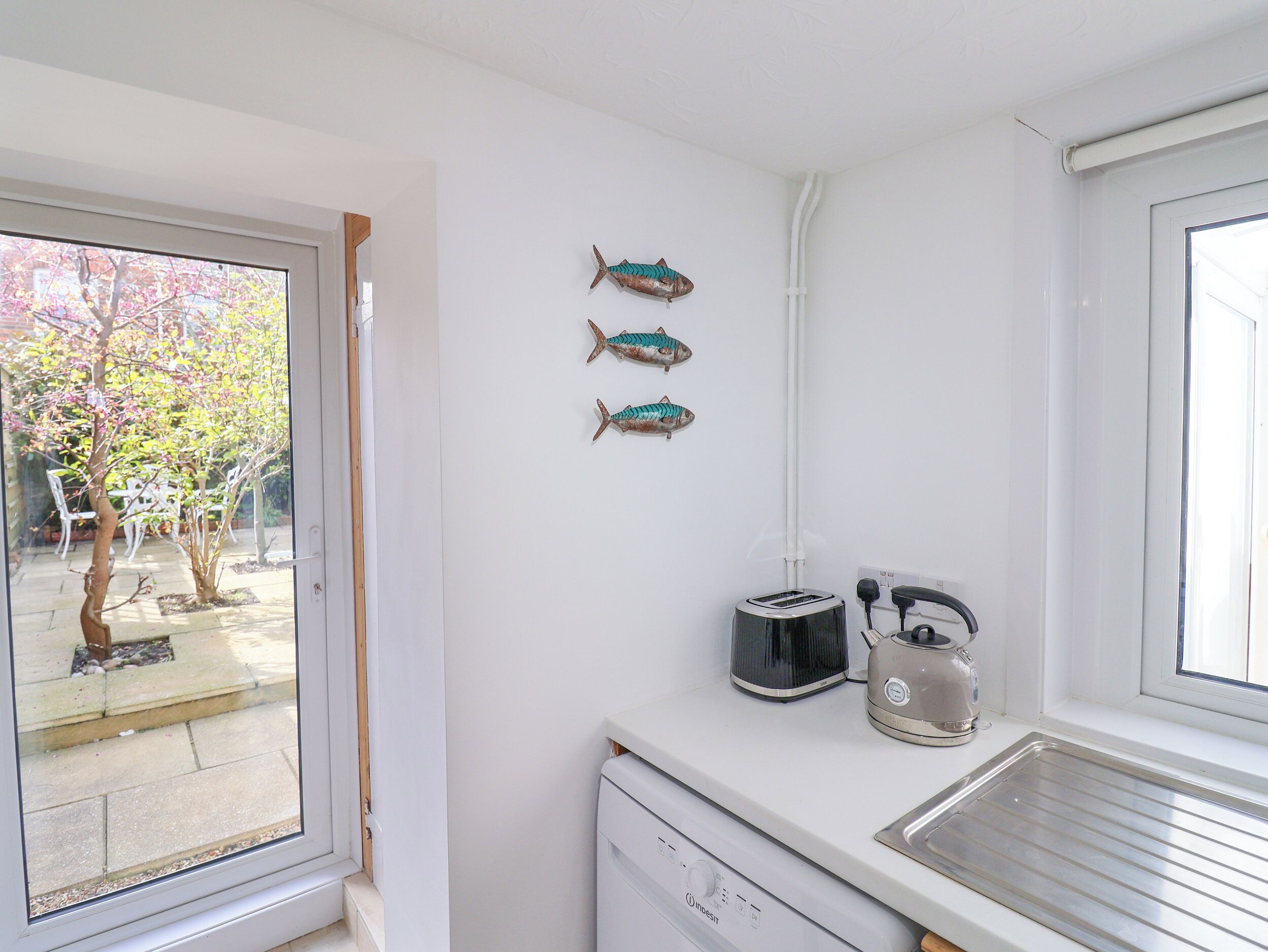 Uma cozinha com janela, torradeira, chaleira e peixes decorativos na parede.