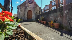 Igreja com uma torre do relógio, caminho pavimentado e plantas em vasos ao longo da parede.