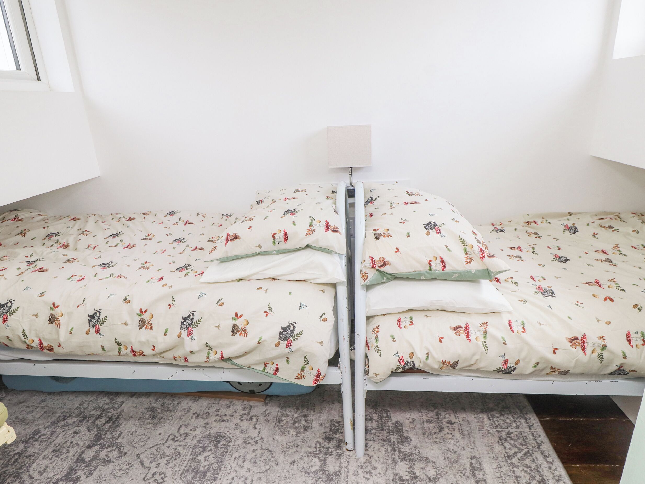 Uma cama pequena com roupa de cama florida, cabeceira branca e piso cinza.