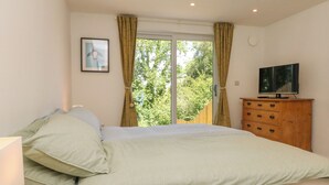 Quarto com cama, cómoda de madeira, televisão e janela com cortinas.