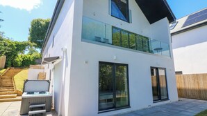 Uma casa moderna de dois andares com varanda, janelas amplas e um pátio com mobiliário externo.