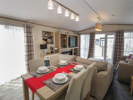 Uma área de jantar com uma mesa posta para quatro pessoas, um sofá e uma televisão ao fundo.