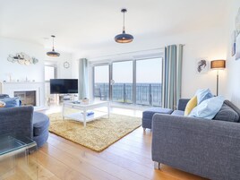 Uma sala de estar moderna com lareira, televisão de tela plana e varanda com vista para o mar.