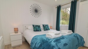 Cama arrumada com toalhas dobradas, manta azul texturizada e um relógio de parede.