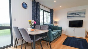Uma sala de estar moderna com uma mesa de jantar, cadeiras, sofá, televisão e um relógio na parede.