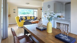 Uma sala de estar moderna com um sofá, uma poltrona amarela, mesa de centro de madeira e um vaso com flores.