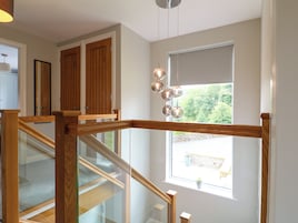 Um interior moderno com escada de madeira, uma janela ampla com vista para o verde e um lustre pendurado.