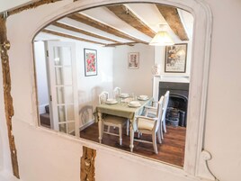 Uma sala de jantar com mesa posta para quatro pessoas, cadeiras brancas, lareira e quadros nas paredes.