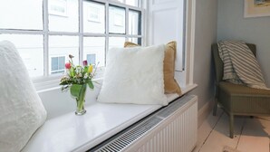 Um quarto com um assento junto à janela, um radiador, uma cadeira e um quadro pendurado na parede.