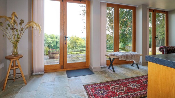 Um quarto amplo com grandes portas de vidro deslizantes que dão para um jardim, um banco de madeira e um vaso com plantas secas.
