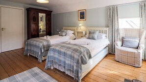 Quarto com duas camas, guarda-roupa de madeira, uma cadeira e uma janela com cortinas.