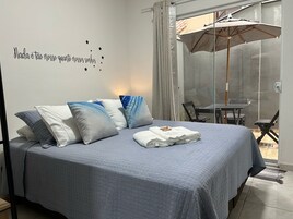 Quarto com cama, almofadas, adesivo na parede e porta de correr de vidro que dá para área externa com mesa e cadeiras.