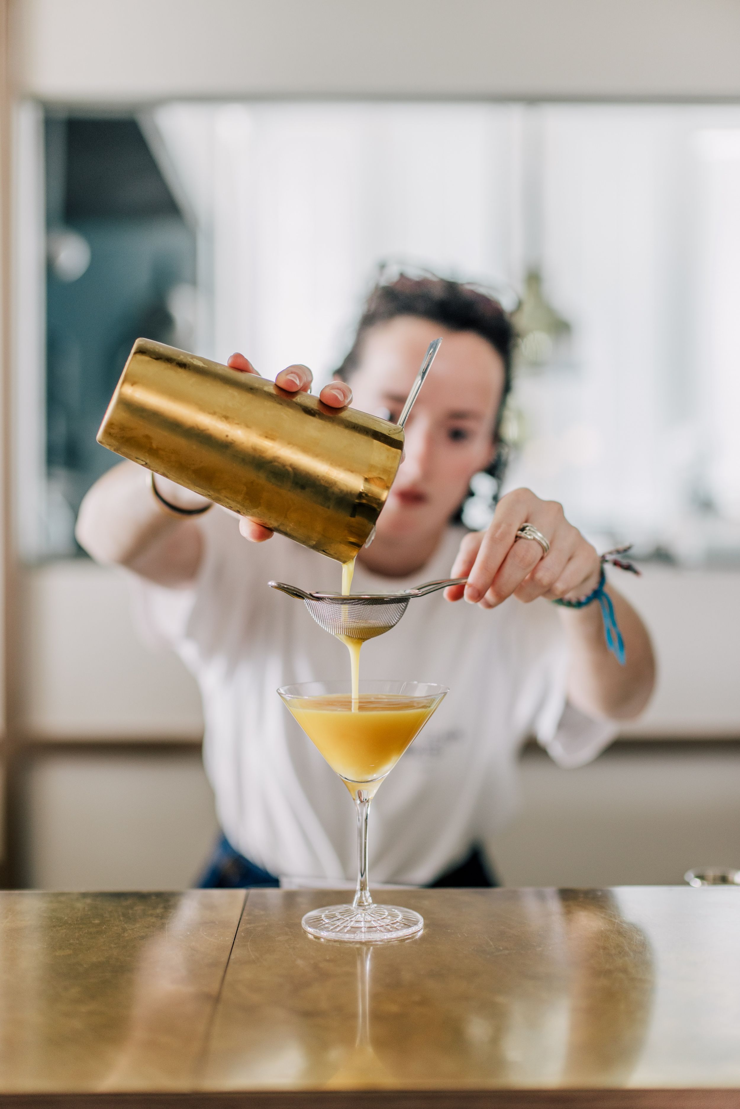 Uma pessoa servindo um líquido dourado em uma taça de martini.