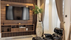 Uma sala de estar moderna com uma grande TV de tela plana fixada numa parede de madeira, um vaso grande com uma planta, duas poltronas de couro e uma mesa de centro de mármore.