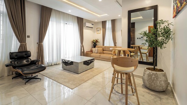 Uma sala de estar moderna com um sofá, uma poltrona de couro preto, uma mesa de centro e um espaço de jantar com uma planta.