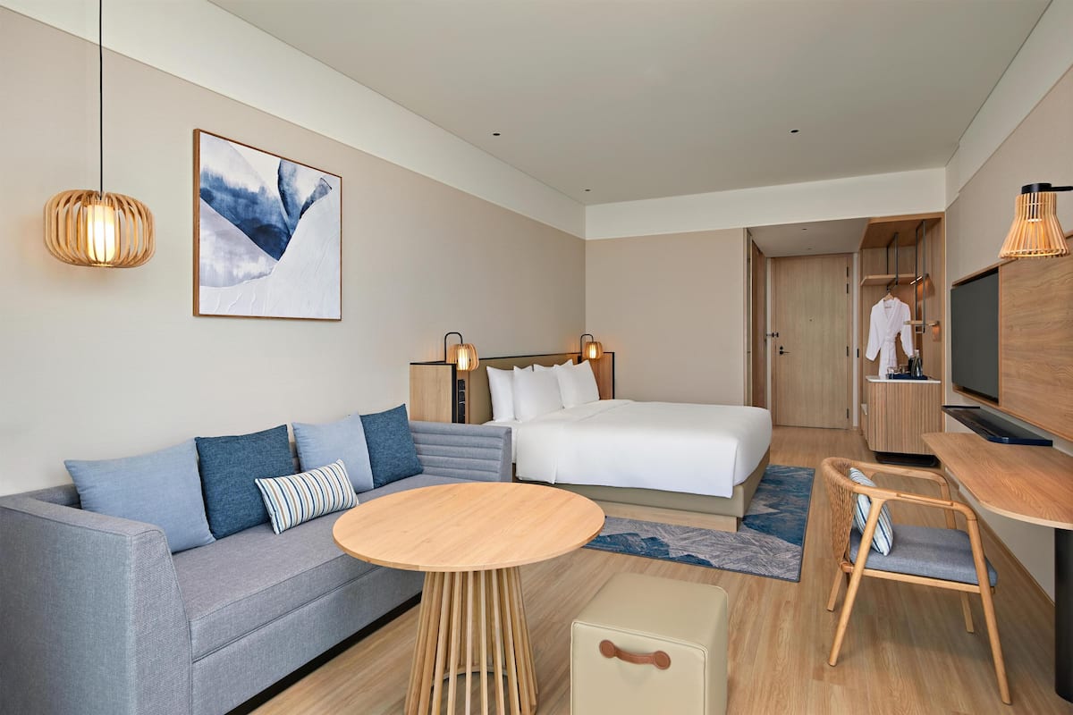 Quarto de hotel moderno com cama, sofá, mesa de madeira e televisão.