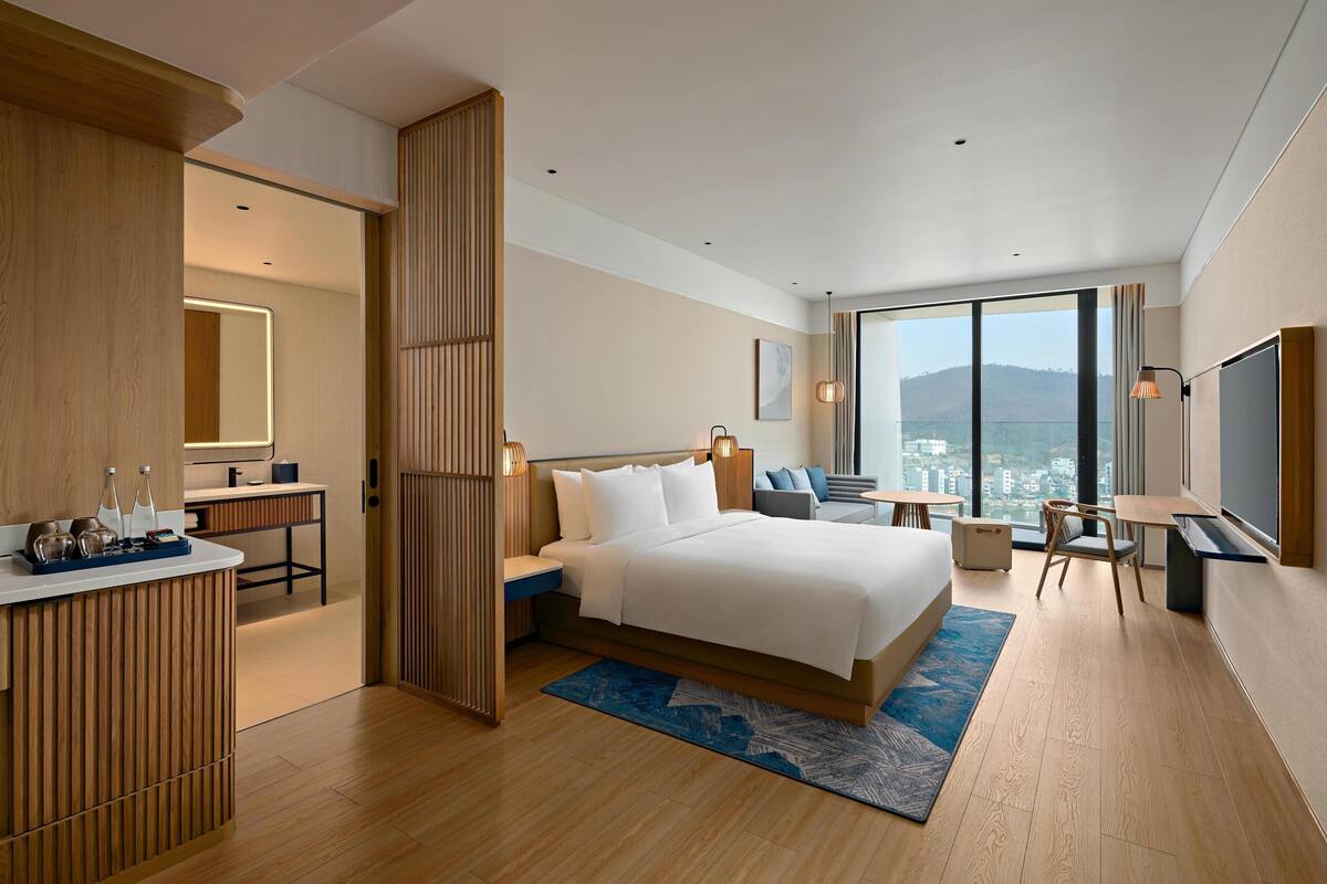 Quarto de hotel moderno com uma cama grande, uma mesa de trabalho e vista para a cidade.