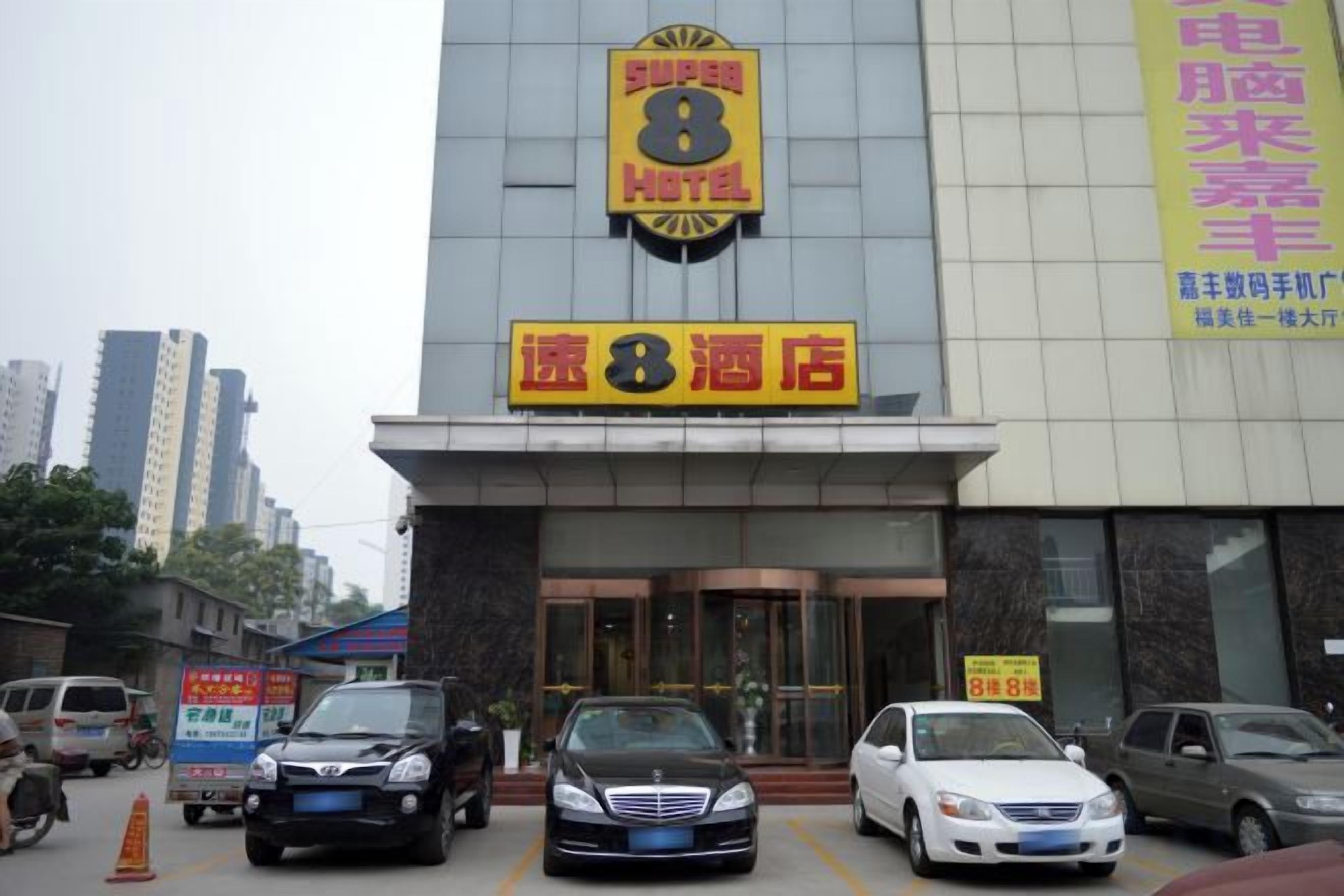 Entrada de um hotel com uma placa chamativa do 'Super 8 Hotel' e um grande anúncio amarelo com uma oferta especial.