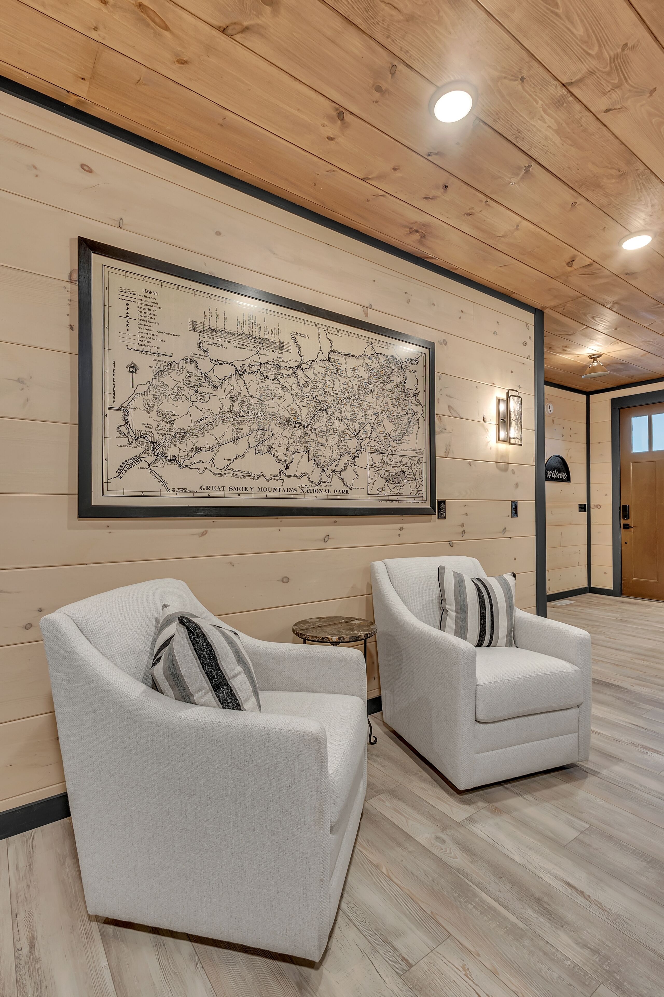 Quarto com paredes de madeira e um grande mapa emoldurado do Parque Nacional das Montanhas Fumegantes. Há duas poltronas brancas com almofadas listradas.