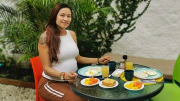 Uma pessoa sentada em mesa ao ar livre, com pratos de comida, um copo de suco de laranja e uma garrafa de suco.
