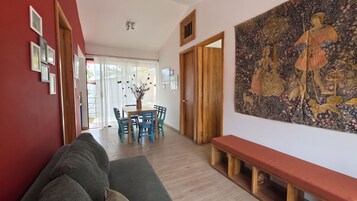 Uma sala de estar moderna com um sofá, um banco de madeira, uma mesa de jantar com cadeiras e uma grande tapeçaria na parede.