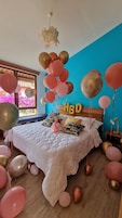Quarto com cama, balões e janela com vista para flores cor-de-rosa.