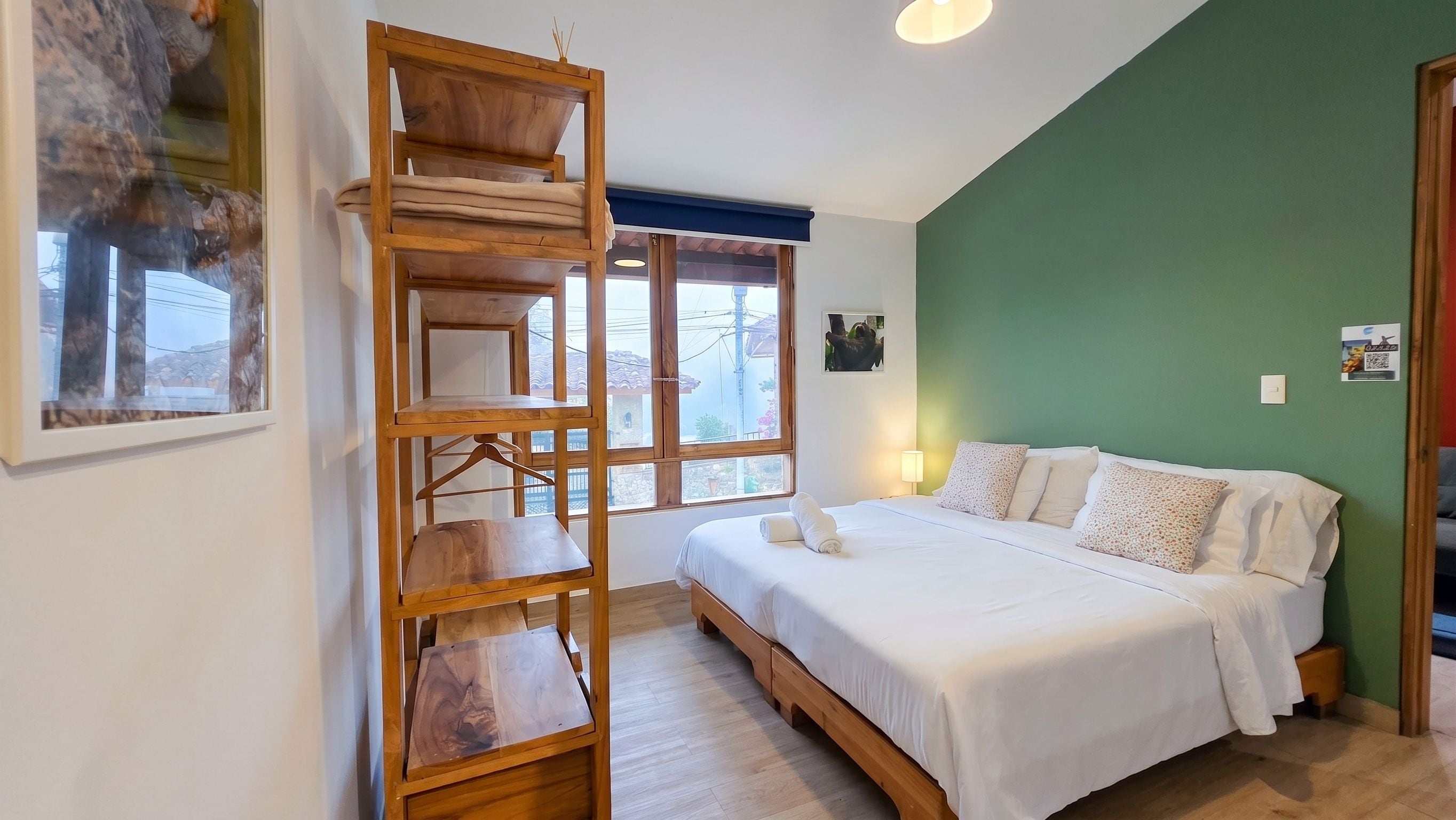 Quarto com uma cama, estante de madeira, janela com vista e parede verde.